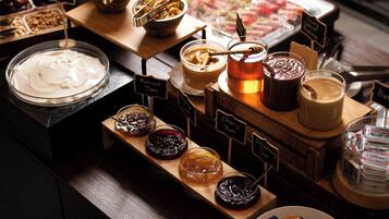 Buffet com diversos alimentos e acompanhamentos, incluindo iogurte grego, iogurte com mel e diferentes geleias.