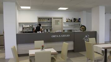 Interior de restaurante com balcão chamado 'ORTA S. GIULIO', área de estar e bar com diversos frascos.