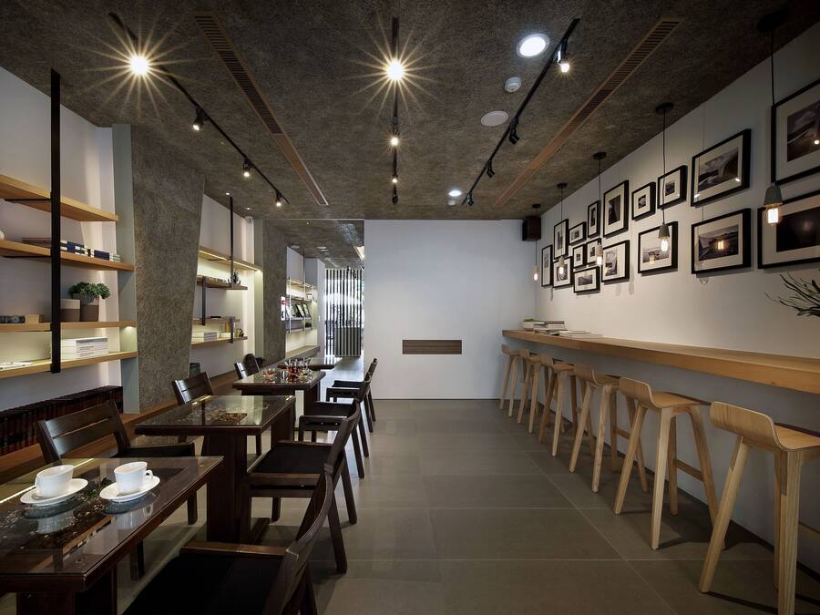 Um café moderno com mesas e cadeiras de madeira, um balcão longo e quadros nas paredes.