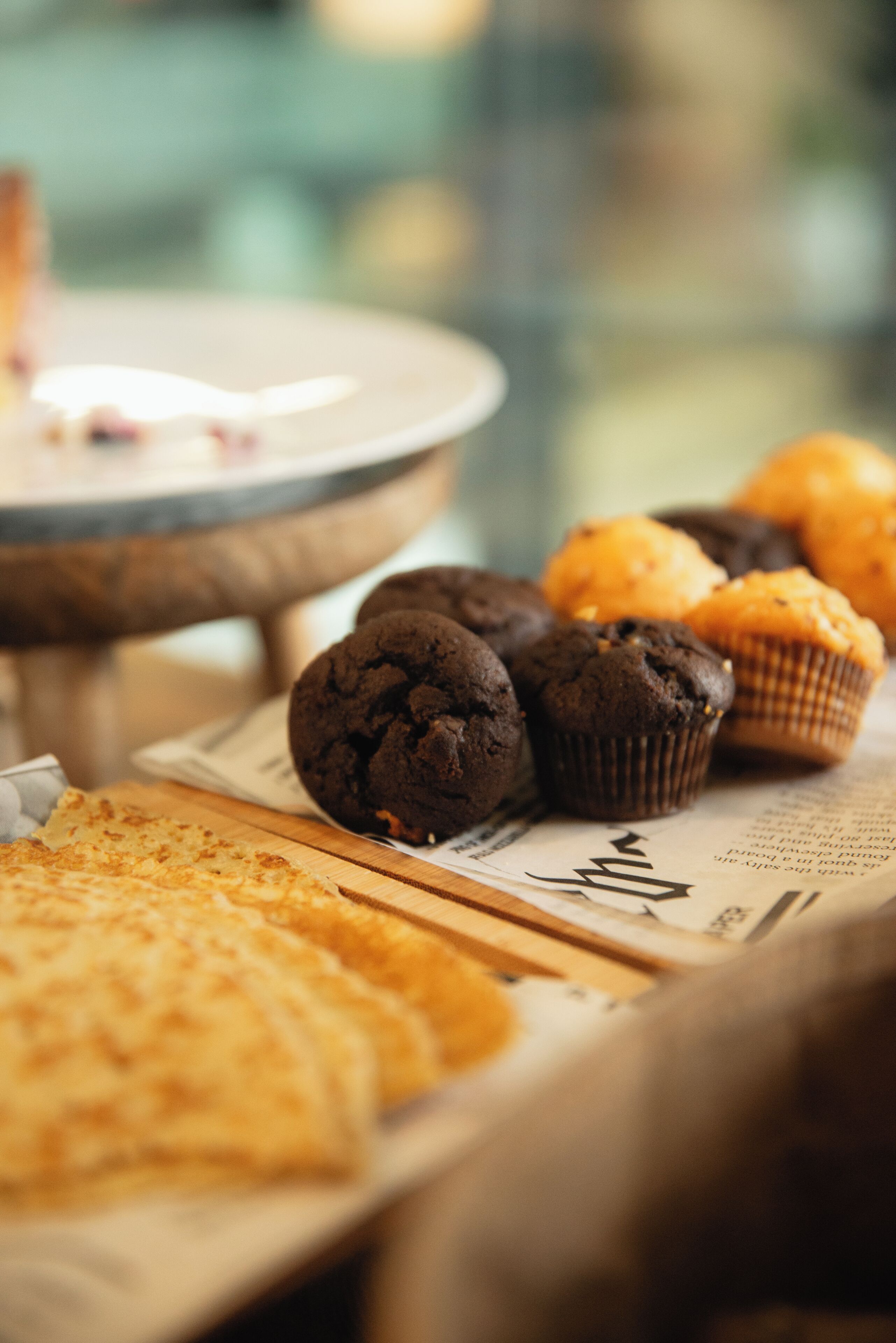 Uma mesa com diversos produtos de pastelaria, incluindo muffins e bolachas, sobre uma superfície com um jornal por baixo.