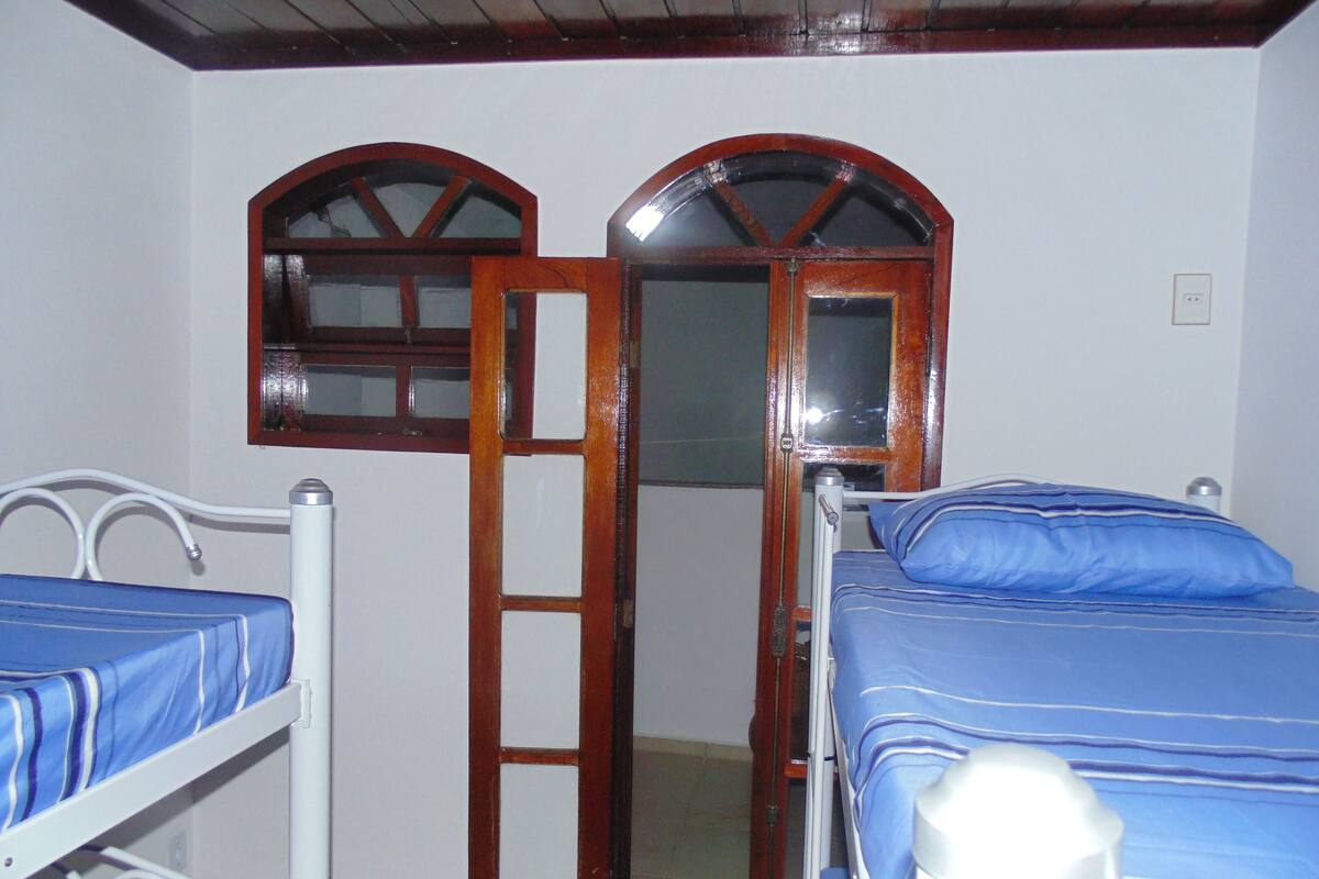 Quarto com duas camas, uma porta de madeira e uma janela.