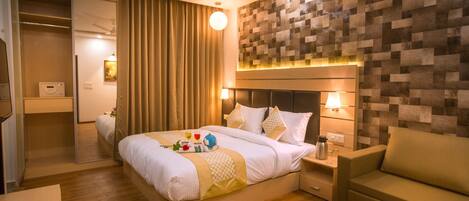 Quarto de hotel moderno com uma cama grande, mesas de cabeceira, um sofá e uma parede com padrão geométrico.
