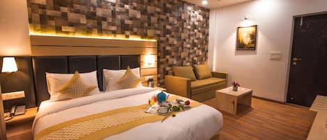 Quarto de hotel com uma cama grande, mesas de cabeceira, um sofá, uma pequena mesa e um ventilador de teto.