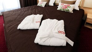 Quarto de hotel com uma cama grande, dois roués brancos com um logotipo e almofadas florais.