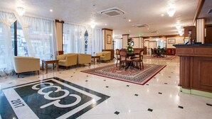 Um saguão de hotel com balcão de recepção, área de estar e um tapete grande.