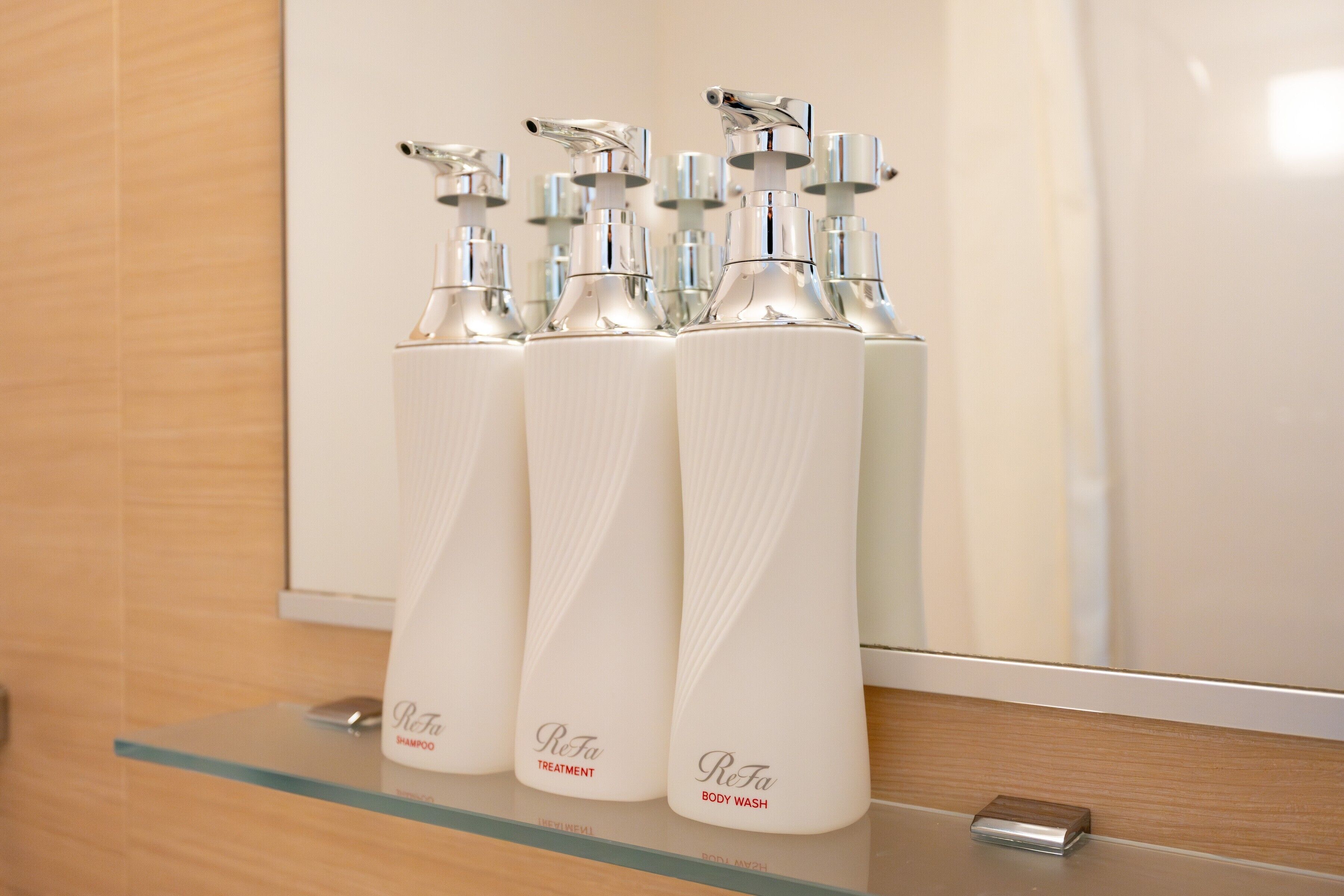Casa de banho com uma prateleira de vidro que exibe três frascos de gel de banho e shampoo ReFa.