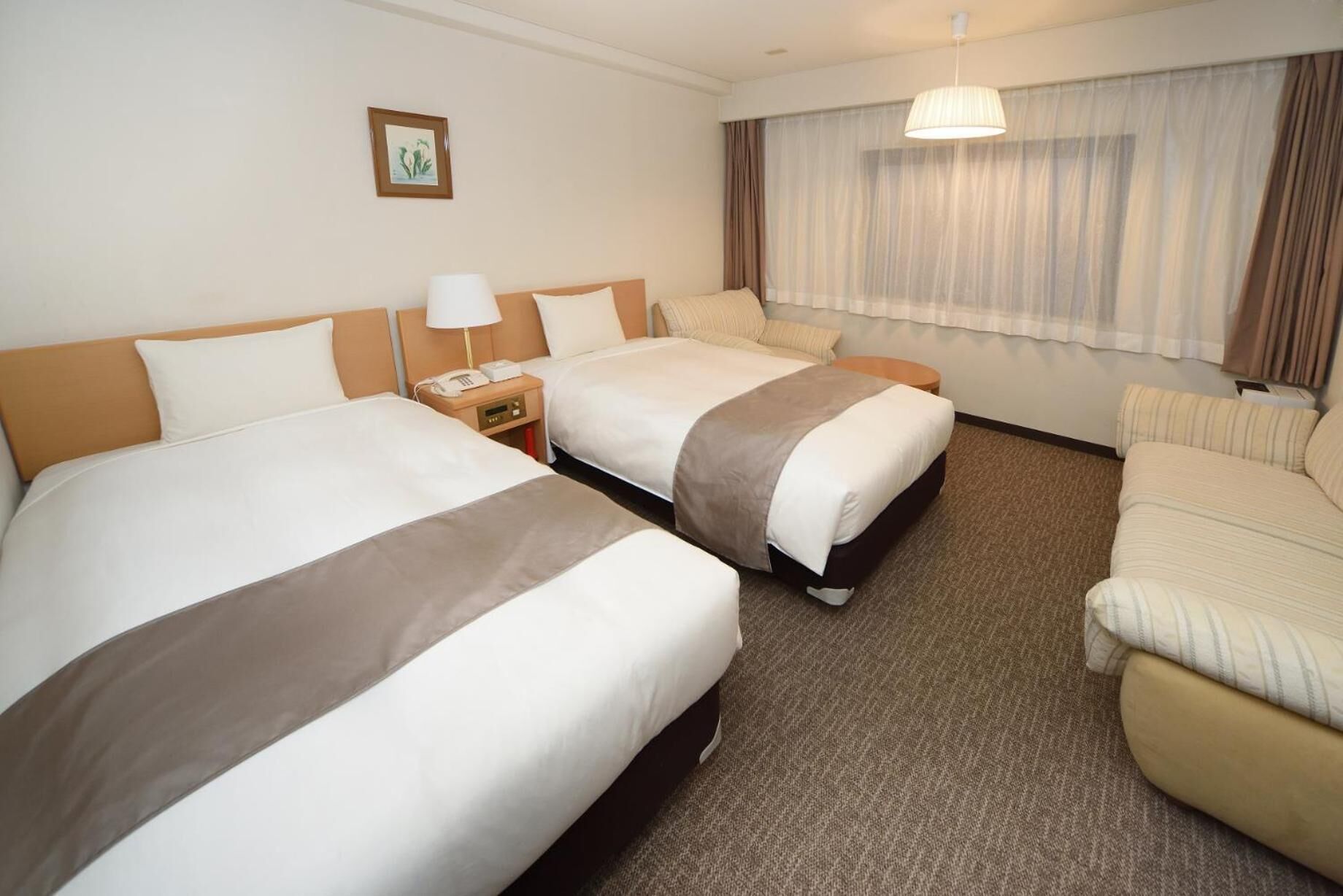 Quarto de hotel com duas camas, uma escrivaninha, uma cadeira, uma luminária e uma janela com cortinas.