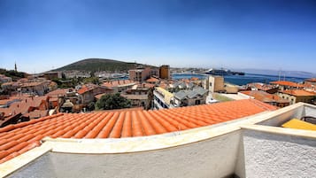 Paisagem costeira urbana com edifícios de telhados em terracota, um porto e uma colina ao fundo.