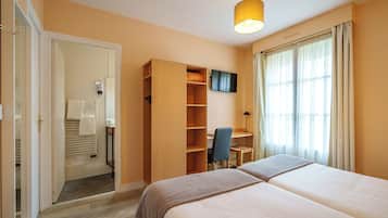 Quarto de hotel com duas camas, uma escrivaninha, uma cadeira, televisão e guarda-roupa.