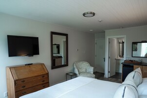 Um quarto com uma cama, penteadeira, cadeira, televisão e espelho.
