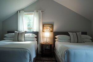 Quarto de hotel com duas camas, uma mesinha de cabeceira com abajur e um quadro na parede.