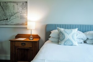 Uma cama bem arrumada com um travesseiro estampado, uma mesa de cabeceira de madeira com uma luminária, e um mapa na parede.
