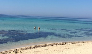 Uma praia com águas turquesa cristalinas e duas pessoas na água.