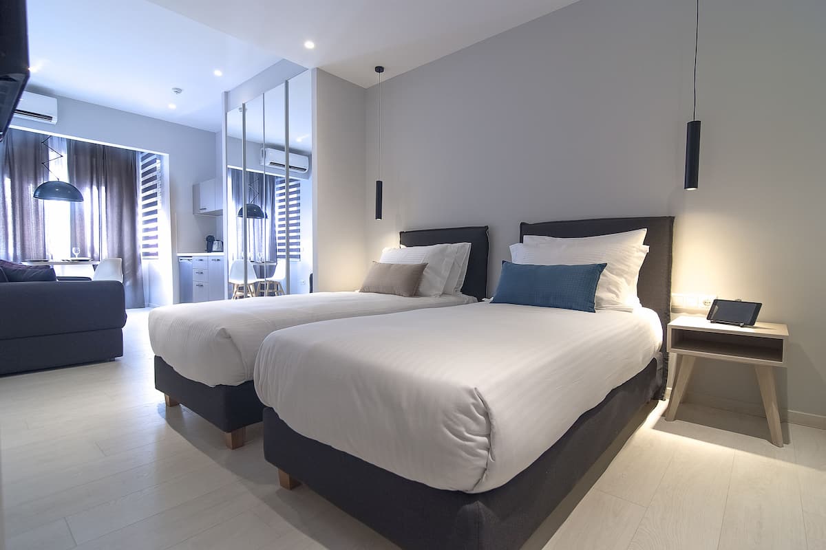 Quarto de hotel moderno com duas camas, um sofá, uma mesa pequena e um espelho.