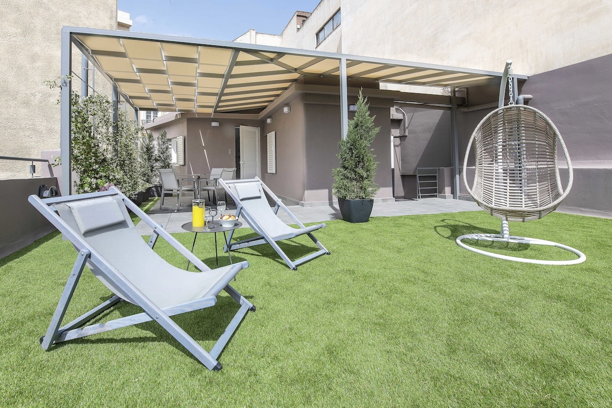 Um terraço no telhado com duas espreguiçadeiras, uma cadeira suspensa e uma pequena mesa com uma bebida.