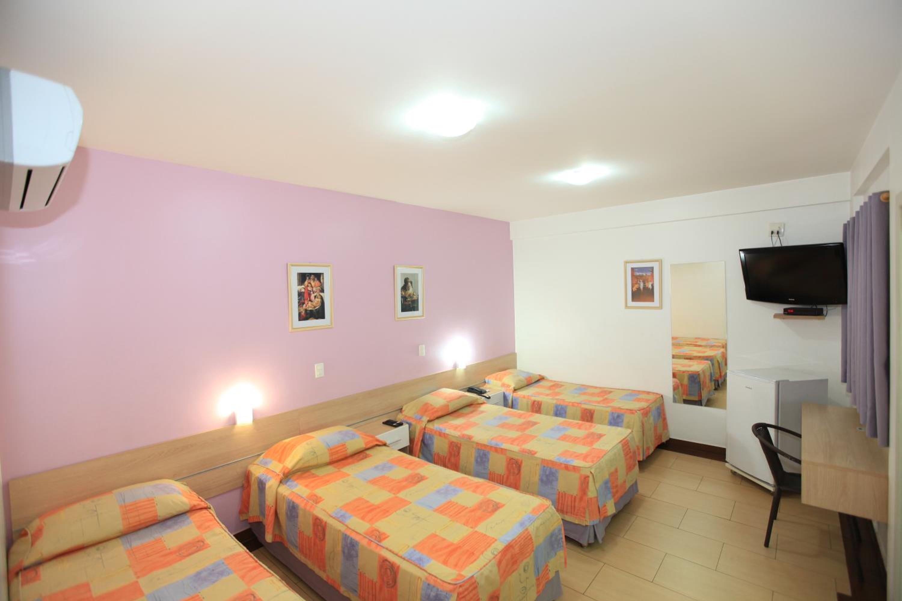 Quarto de hotel com quatro camas, televisão, escrivaninha e uma cadeira.