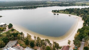 Vista aérea de um lago com praia de areia, rodeado por árvores e alguns edifícios.