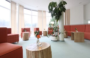 Um hall moderno com assentos vermelhos, mesas de madeira e plantas em vasos.