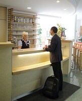 Bancada de recepção de madeira com prateleiras acima, contendo copos e garrafas.