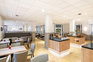 Um restaurante moderno com um balcão central de madeira, várias áreas de estar e um teto limpo revestido de azulejos.