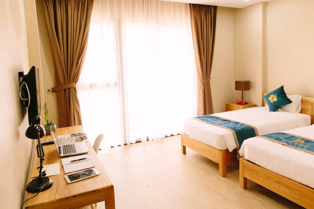 Quarto de hotel com duas camas, uma mesa de escritório, um laptop, uma luminária e um vaso de plantas.
