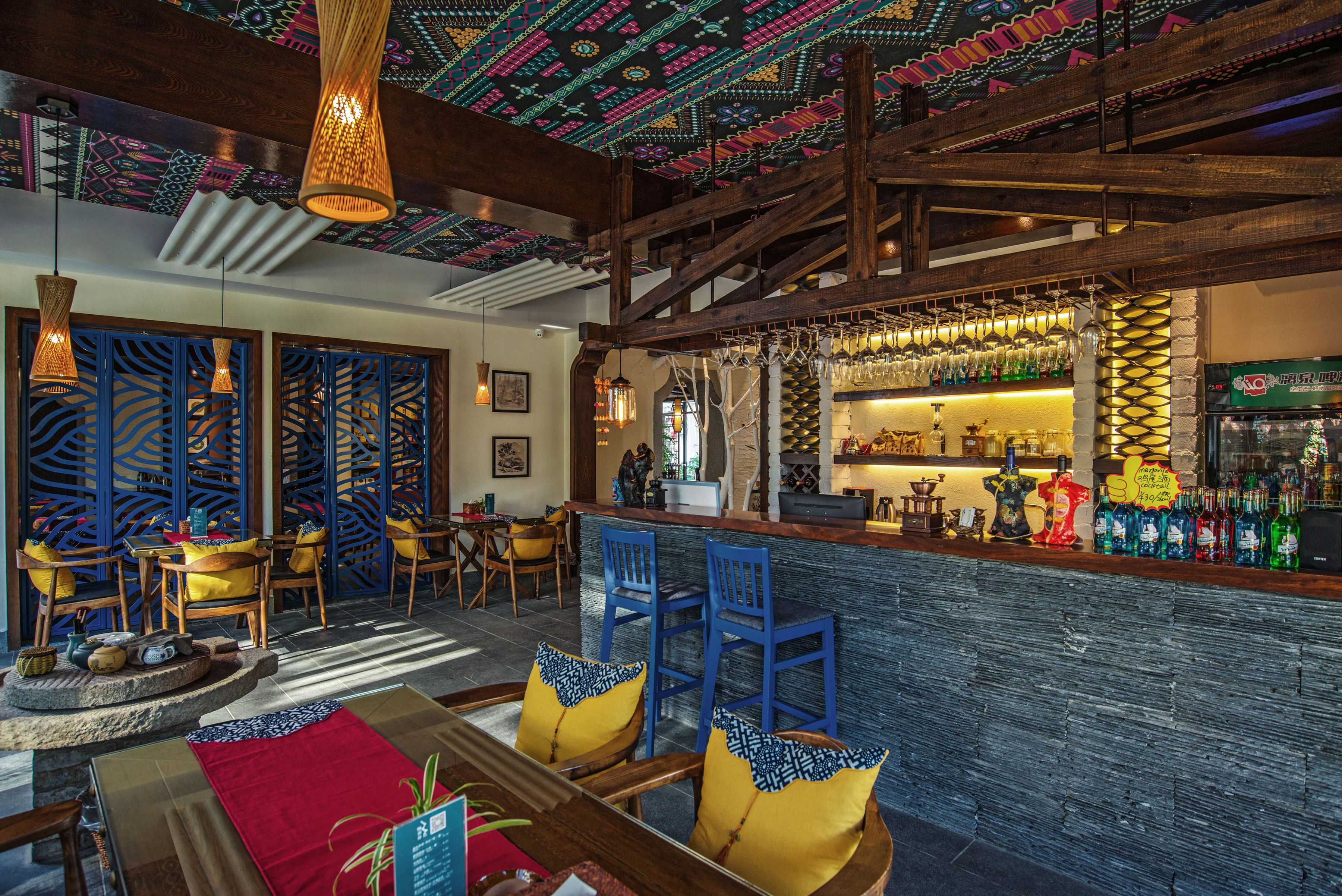 Uma área de bar com cadeiras de madeira, balcão com garrafas e teto decorativo.
