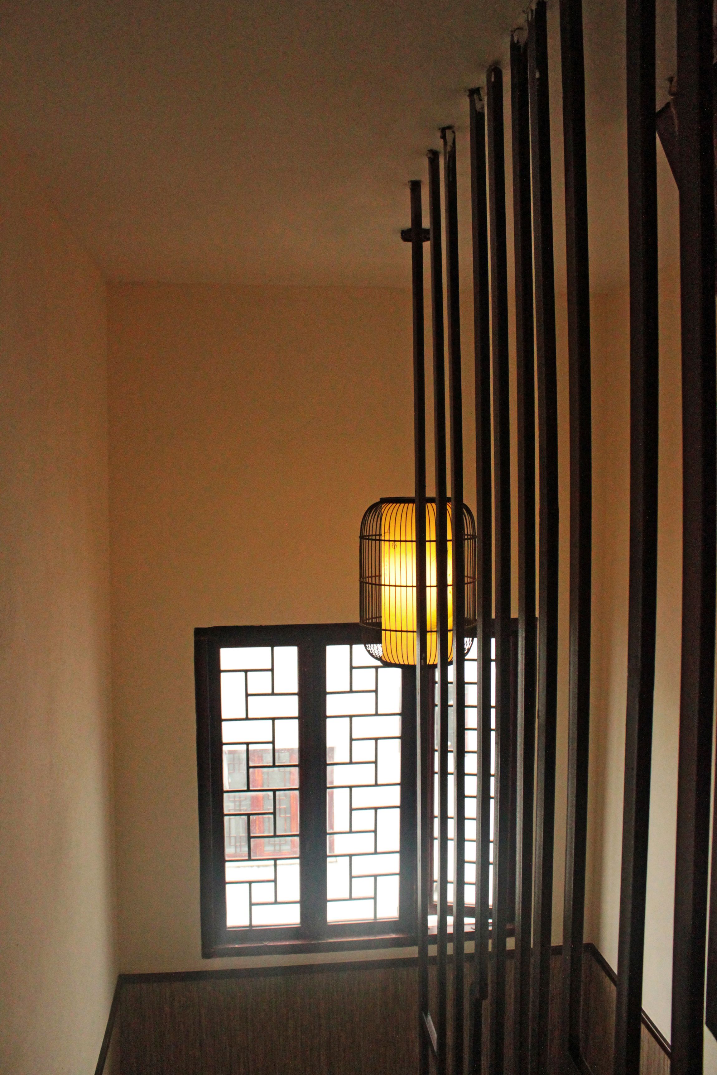 Uma escadaria com um candeeiro tradicional e uma janela com padrão quadriculado.