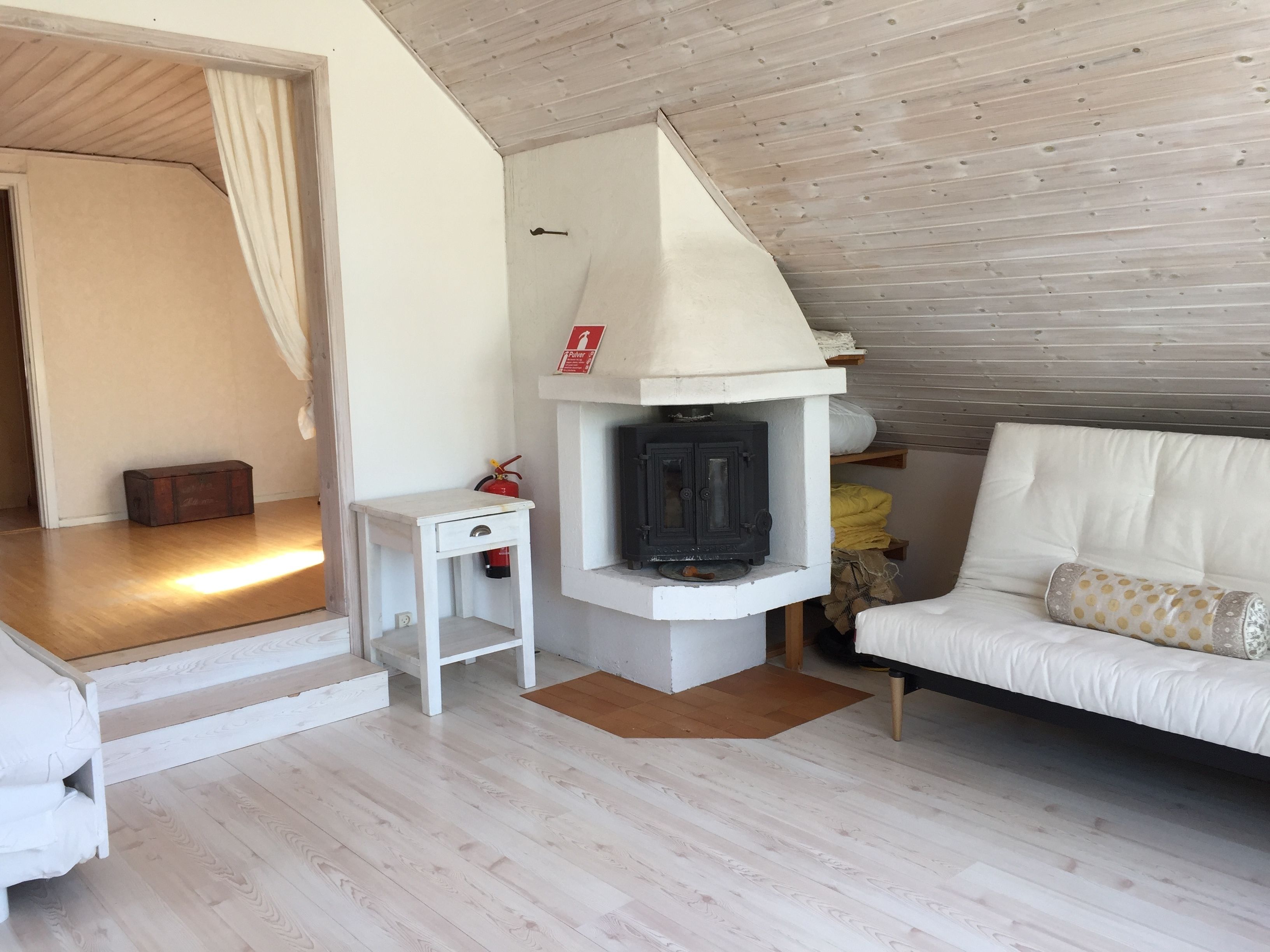 Uma sala de estar acolhedora com um sofá branco, uma mesinha pequena branca, uma lareira e teto de madeira.