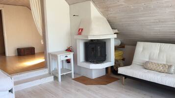 Uma sala de estar acolhedora com um sofá branco, uma mesinha pequena branca, uma lareira e teto de madeira.