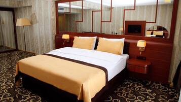 Quarto de hotel com uma cama grande, cabeceira de madeira, um espelho, mesa de cabeceira e piso coberto de carpete.