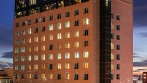 Um hotel moderno com vários andares, um letreiro chamativo no topo e uma grande área de estacionamento em frente.