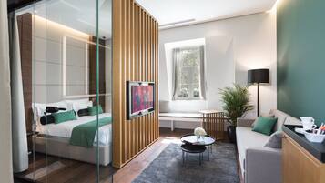 Quarto de hotel moderno com cama, sofá, mesa pequena e janela.