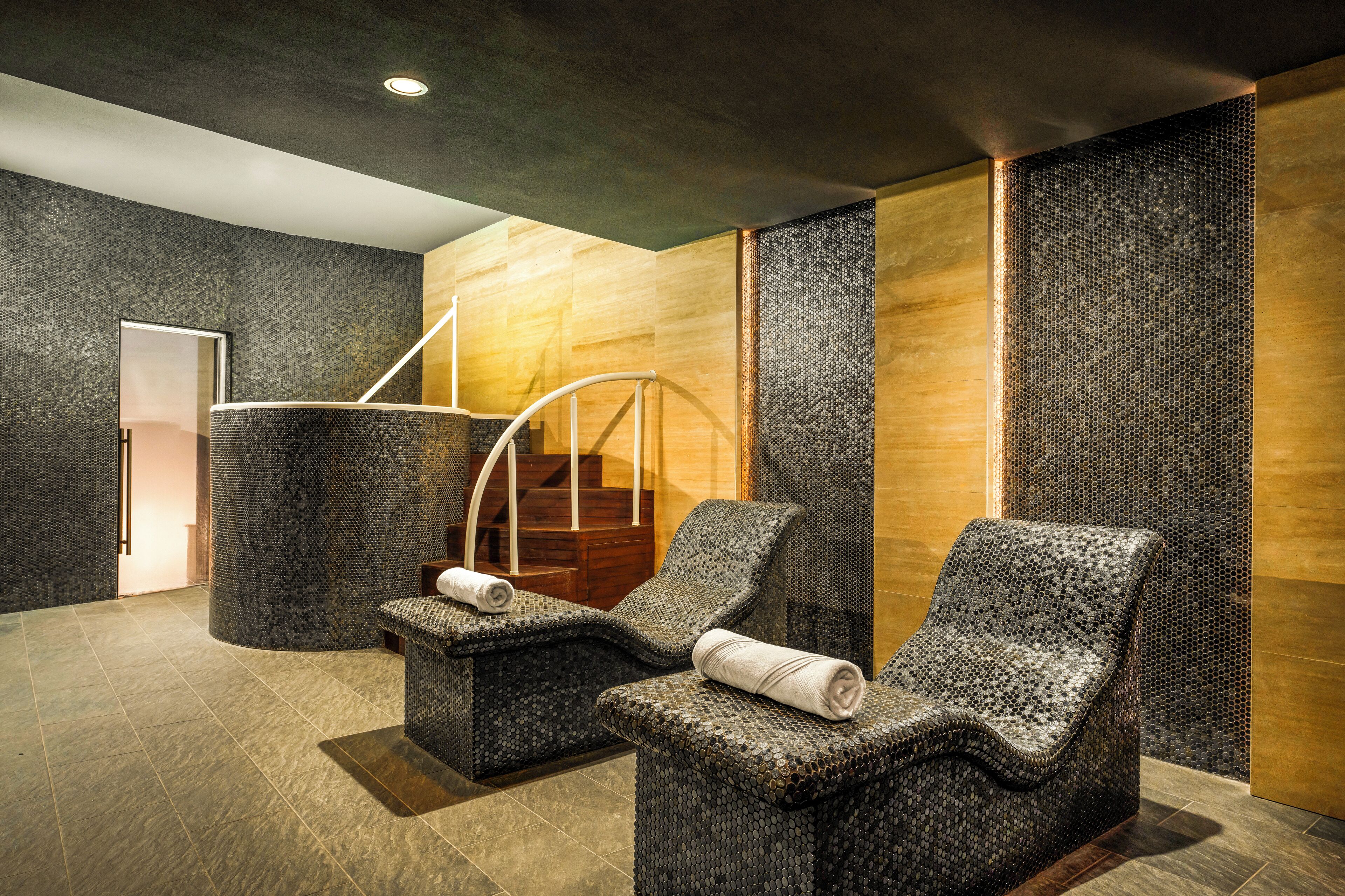 Espaço de spa com duas cadeiras de massagem, uma escada de madeira e uma parede texturizada.