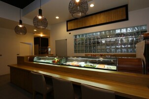 Uma área de bar moderna com balcão de madeira, vitrines de vidro e luminárias pendentes.