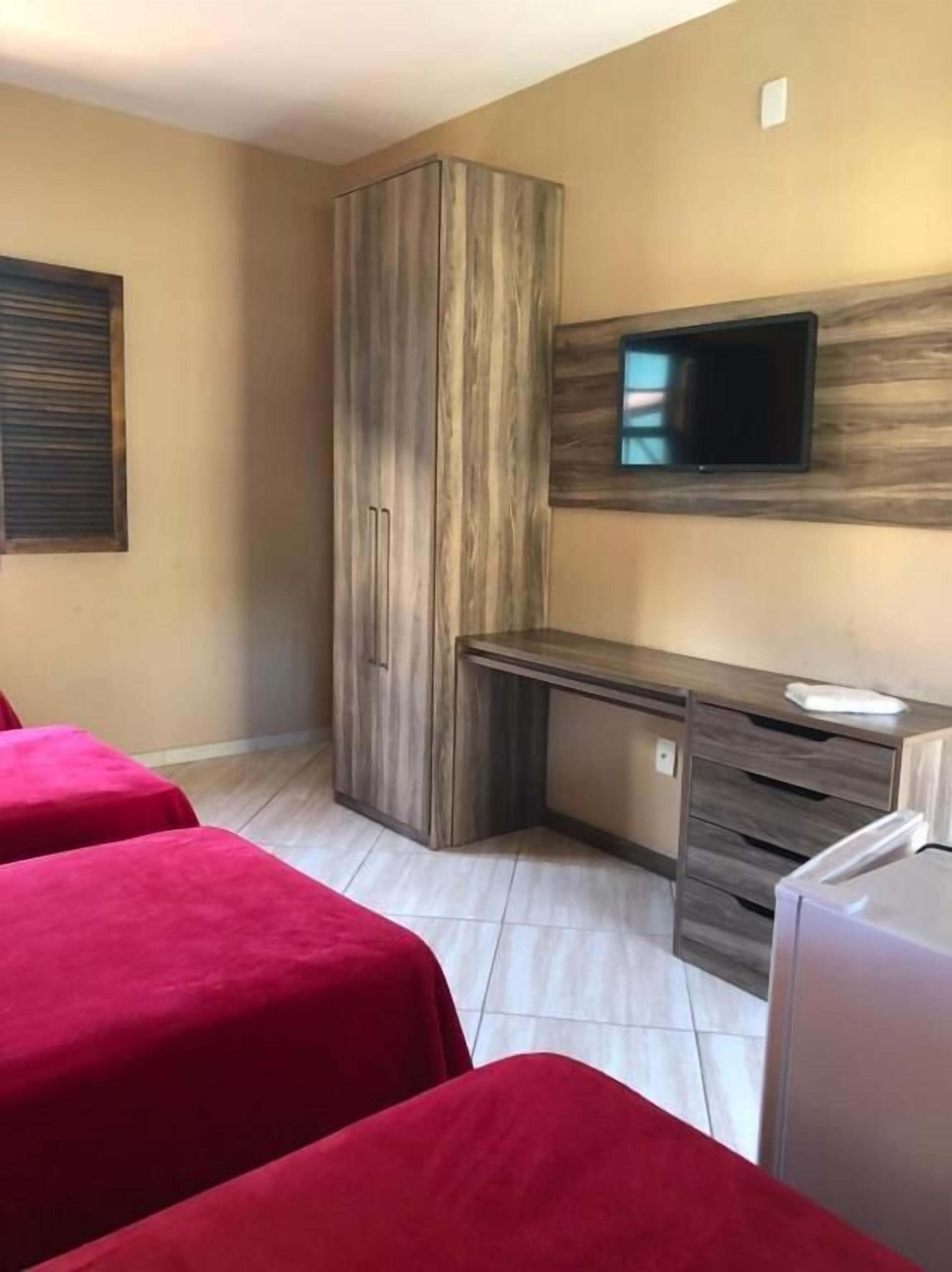 Quarto com cama, escrivaninha, guarda-roupa e televisão.