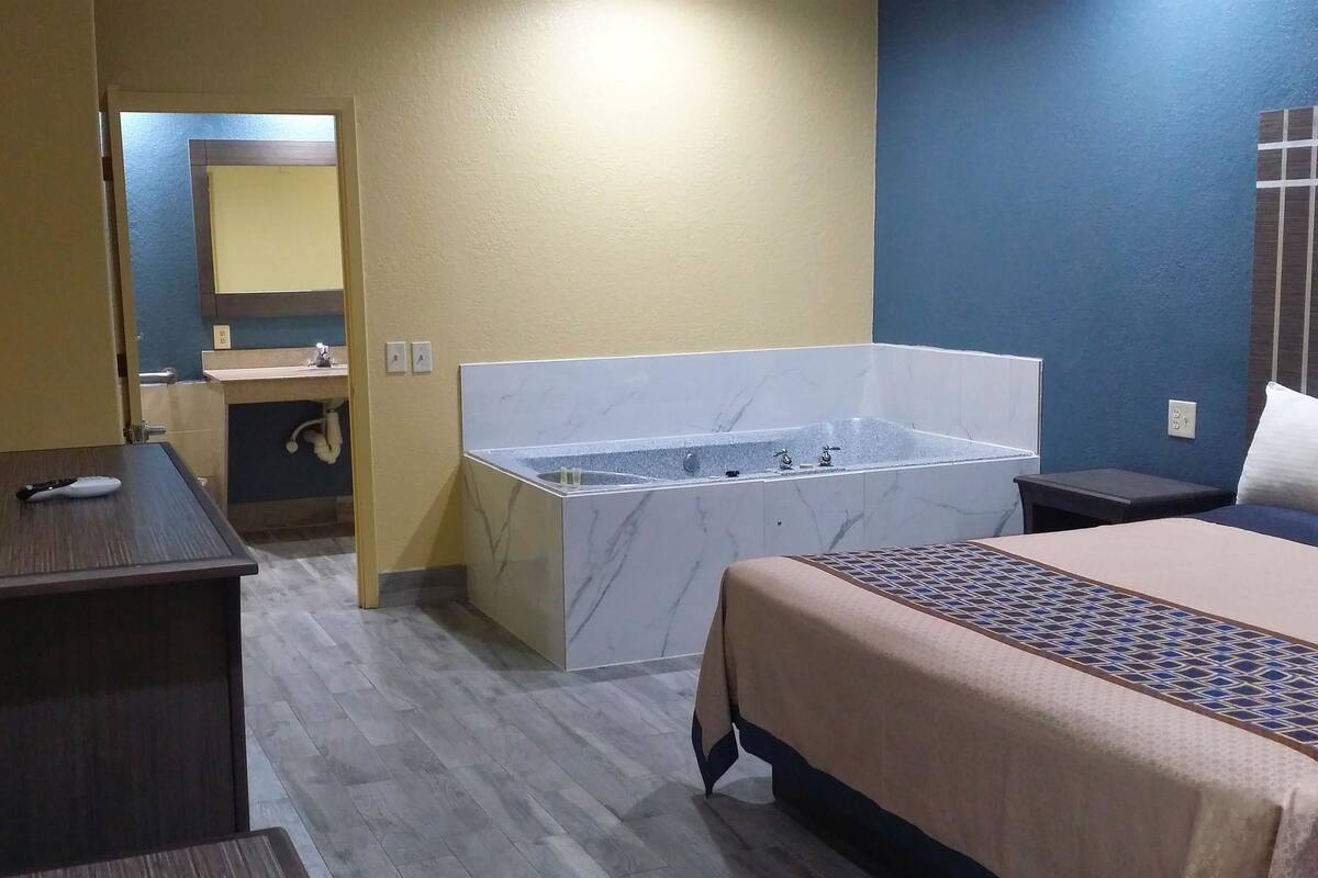 Quarto de hotel com cama, escrivaninha, banheiro com banheira e uma pequena mesa.