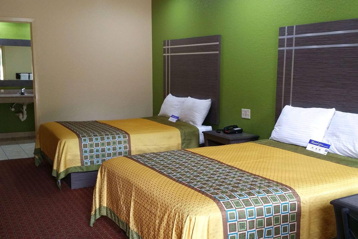Quarto de hotel com duas camas, uma mesa de cabeceira, um espelho e uma pia.
