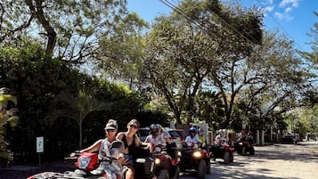 Um grupo de pessoas andando em veículos todo-terreno em uma estrada cercada por árvores.