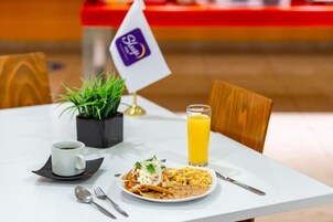 Uma mesa de jantar com um prato de comida, um copo de suco de laranja, uma xícara de café e uma pequena planta.