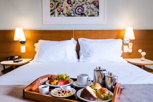 Quarto de hotel com uma cama bem arrumada, uma bandeja com itens de café da manhã e um quadro na parede.