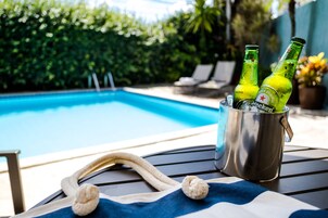 Cenário à beira da piscina com um balde de metal contendo duas garrafas de Heineken, uma bolsa listrada em azul e branco e uma cadeira de metal.