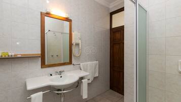 Uma casa de banho com lavatório, espelho e chuveiro.
