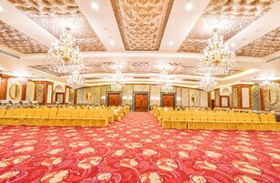 Uma sala de conferências ampla com fileiras de cadeiras amarelas, decoração de teto elaborada e lustres.