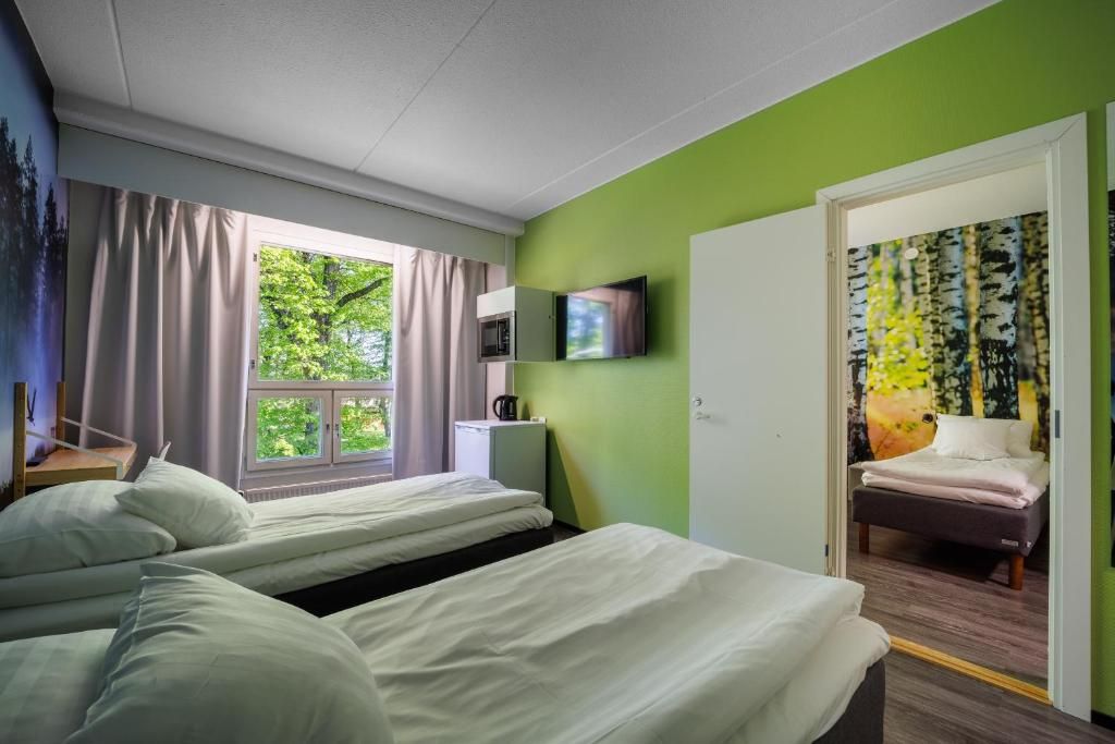 Quarto de hotel com duas camas, televisão, janela com cortinas e porta que dá para outro cômodo.
