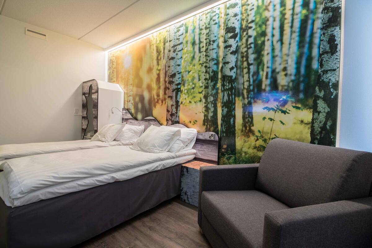 Quarto com cama, sofá e um mural na parede com uma floresta.