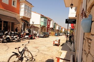 Rua com motocicletas estacionadas e uma bicicleta, placa com 'Eldoris Hotel' e um edifício com fachada de pedra.