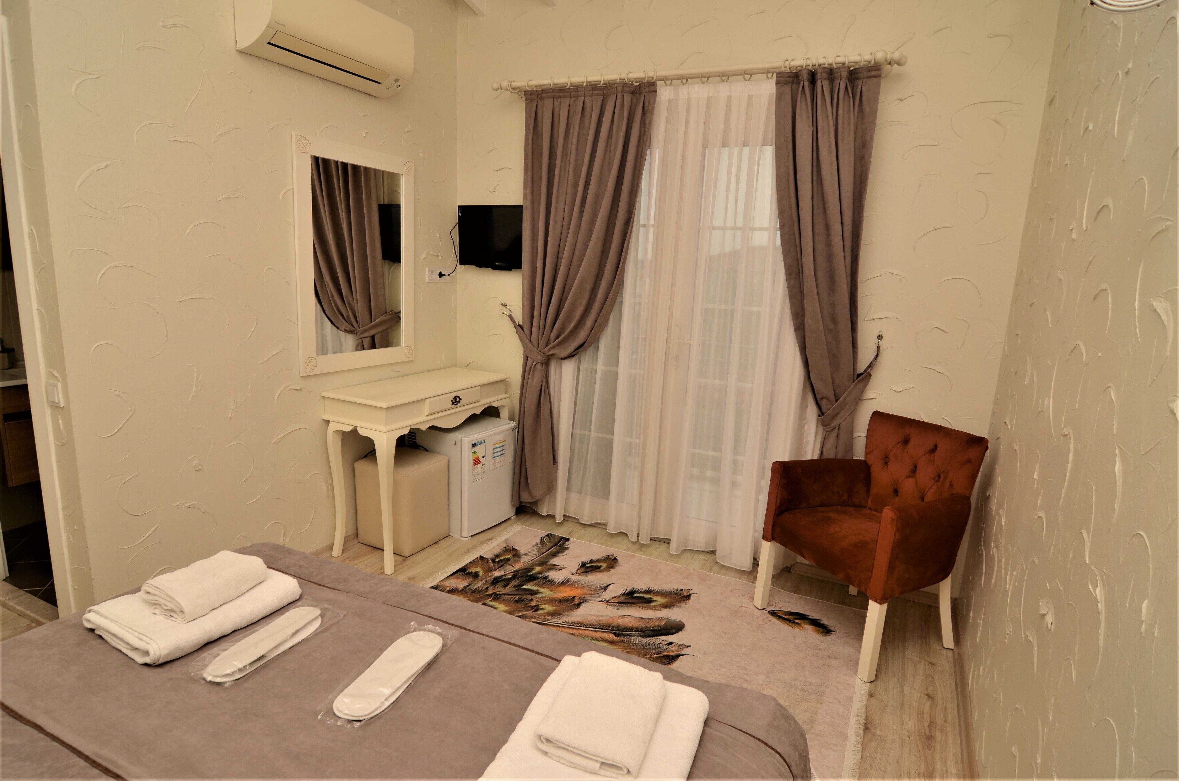 Quarto com cama, cadeira, penteadeira com espelho e janela com cortinas.