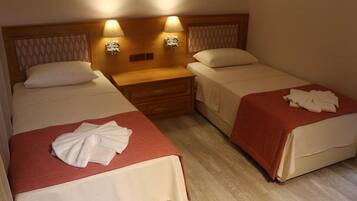 Quarto de hotel com duas camas de solteiro, uma mesinha de cabeceira de madeira e duas luminárias fixadas na parede.