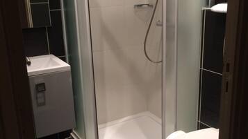 Um banheiro moderno com chuveiro em cabine de vidro, vaso sanitário branco e pia.