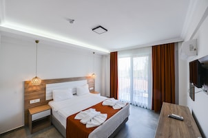 Quarto de hotel moderno com uma cama grande, mesa de cabeceira de madeira, escrivaninha e televisão fixada na parede.